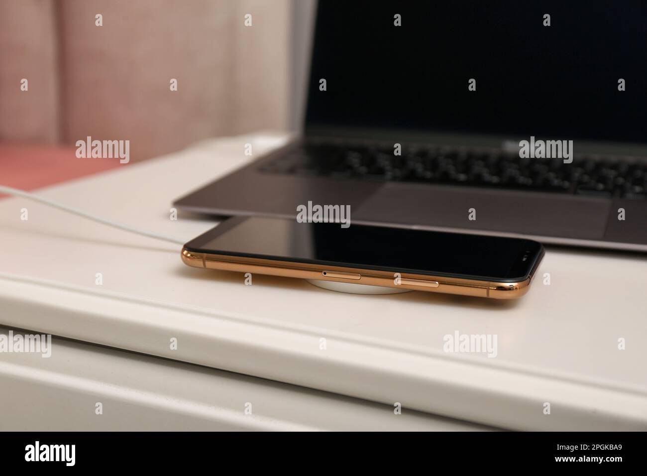 Smartphone with wireless charger connected to laptop on white table ...