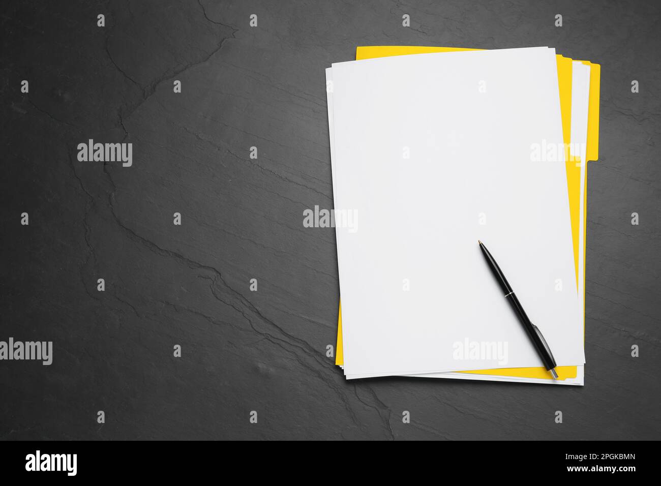 Yellow file with blank sheets of paper and pen on black slate table ...