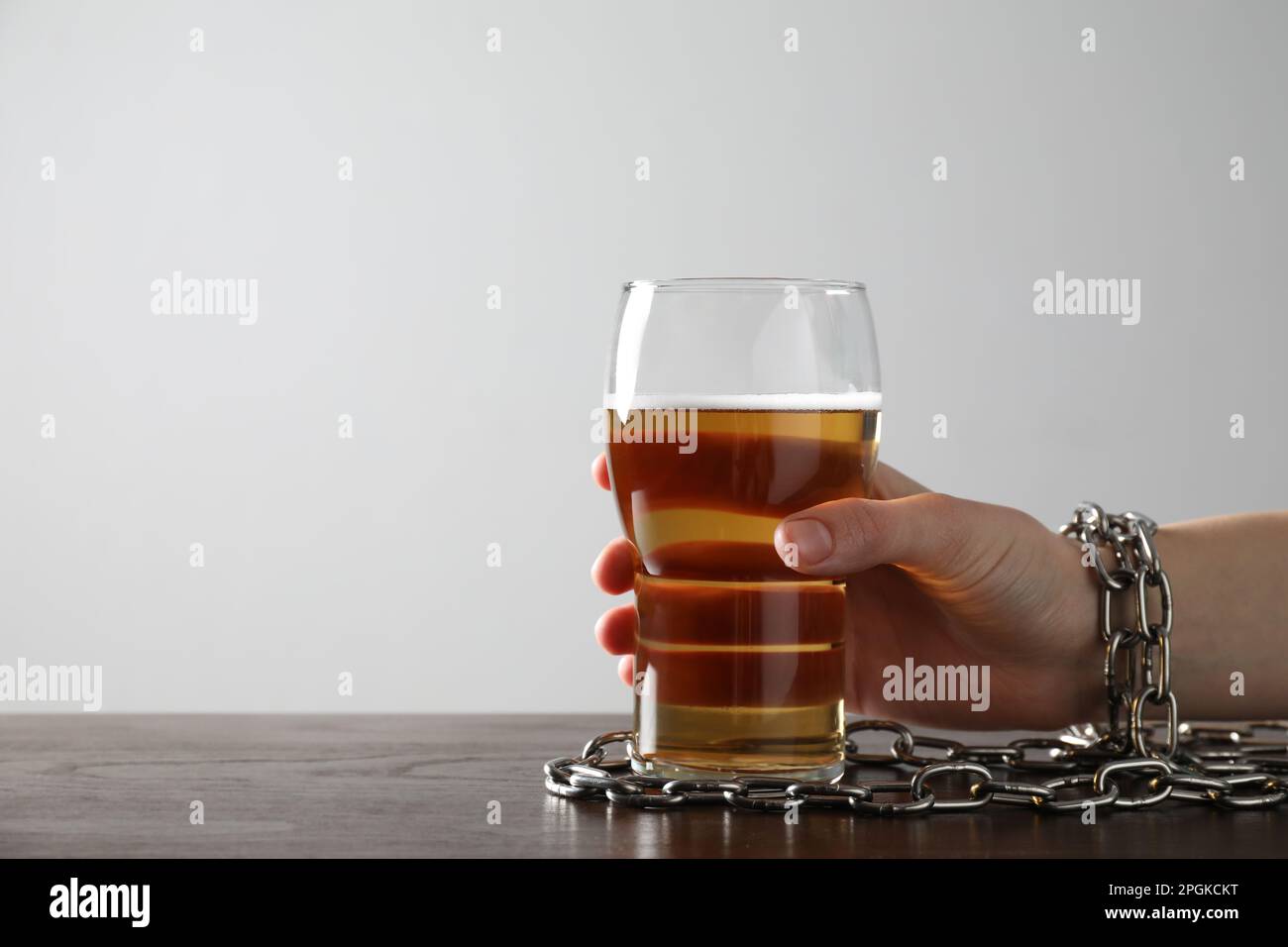 Woman with chained hand and glass of beer at wooden table against white ...