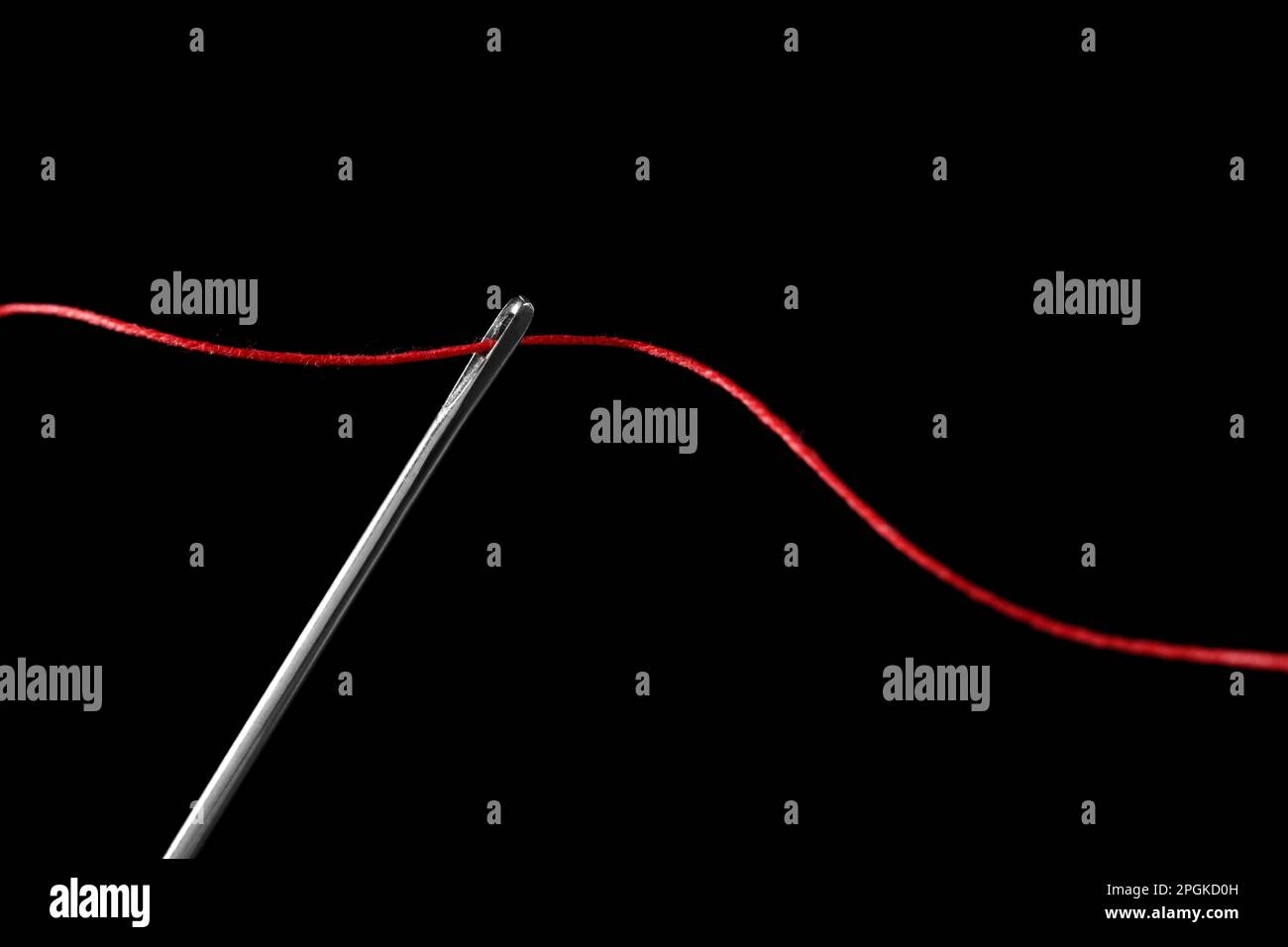 Sewing needle with red thread on black background Stock Photo - Alamy