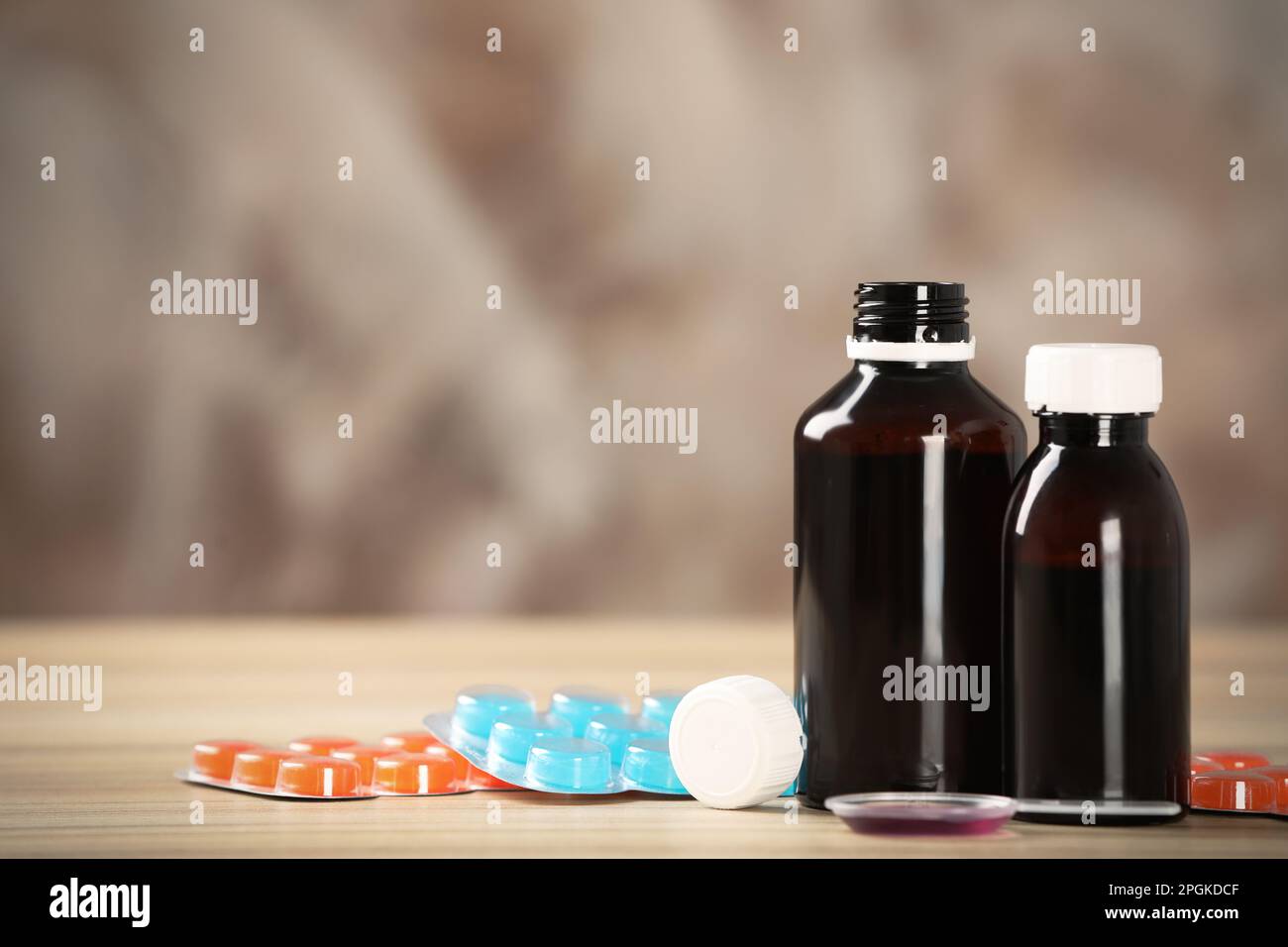 Bottles of syrup, dosing spoon and cough drops on wooden table. Space ...