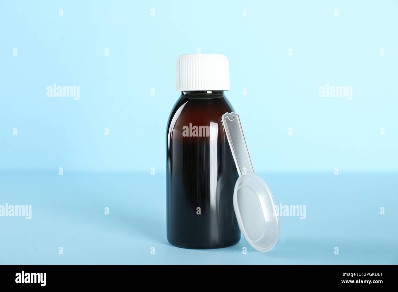 Bottle of cough syrup and dosing spoon on light blue background Stock ...