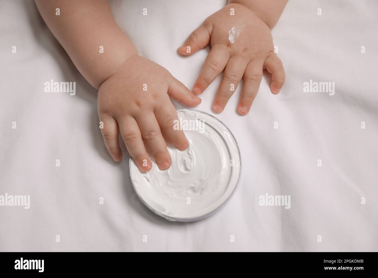 Cute little baby playing with jar of moisturizing cream on bed, closeup ...