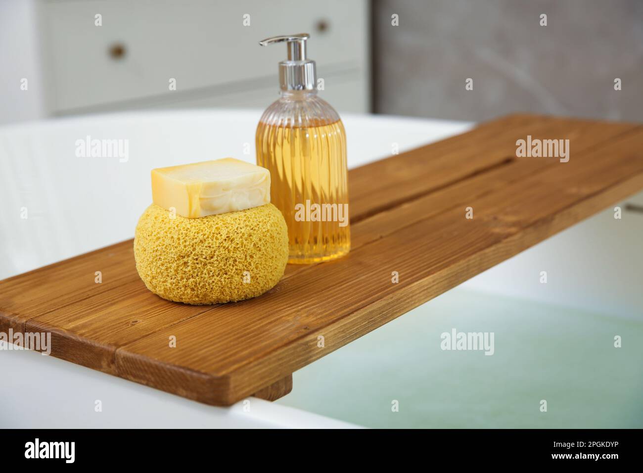 Wooden bath tray with sponge, soap bar and dispenser on tub Stock Photo ...