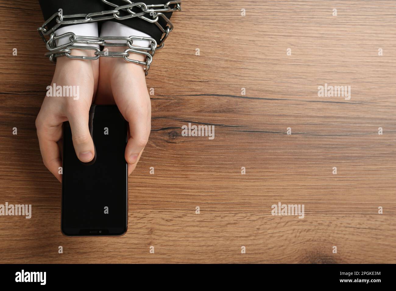 Man holding smartphone in chained hands at wooden table, top view ...