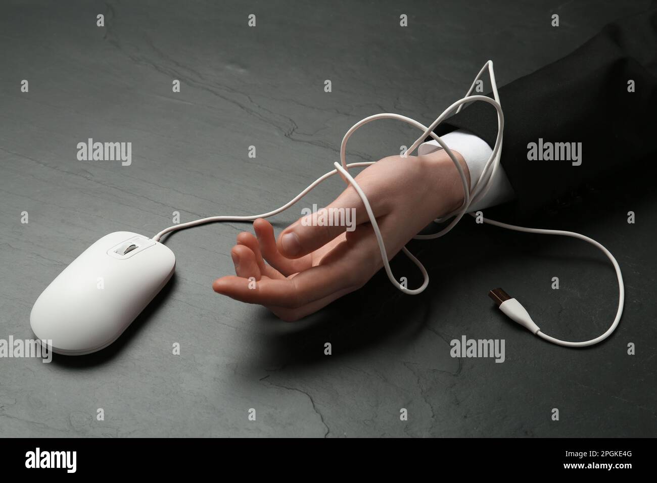 Man tied with computer mouse cable at black table, closeup. Internet ...