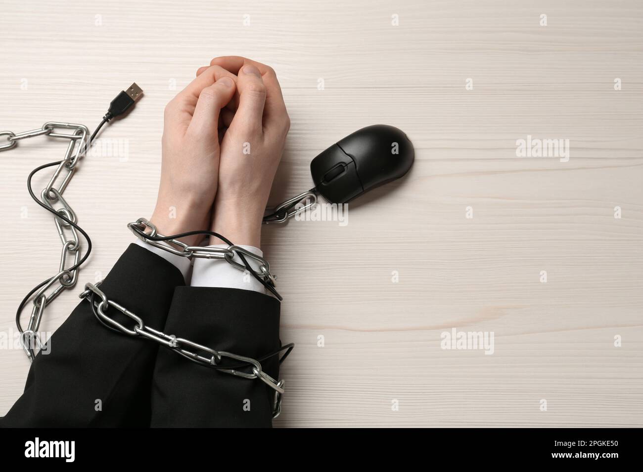 Man showing hands chained with computer mouse cable at white wooden ...