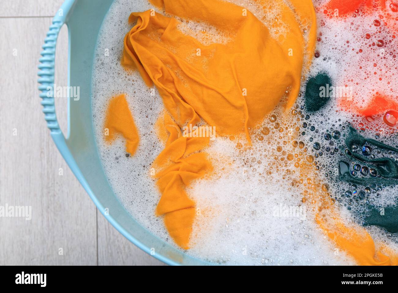 Basin with colorful clothes in suds on floor, top view. Hand washing ...