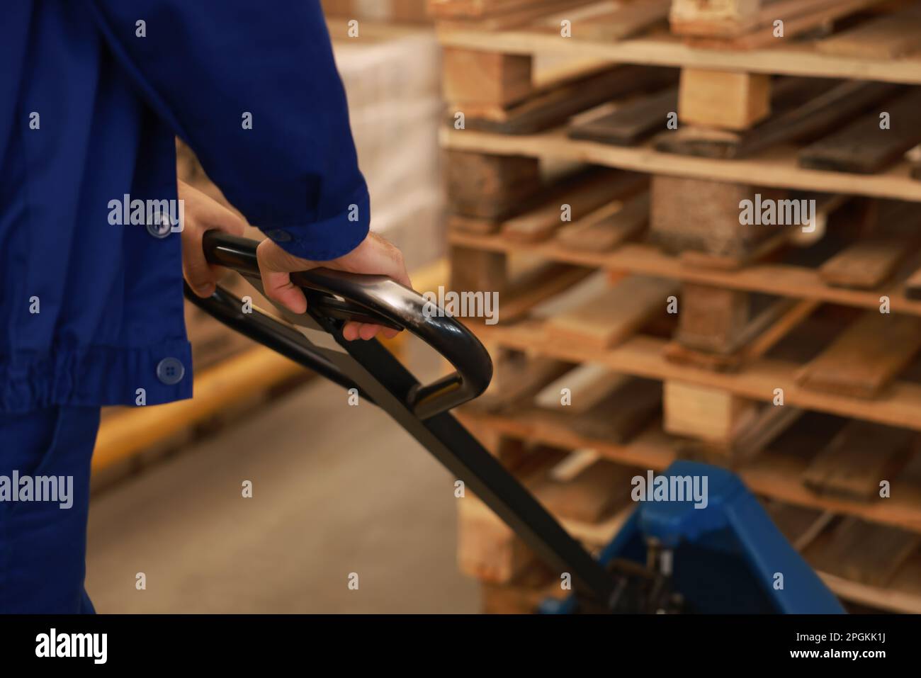 Worker moving wooden pallets with manual forklift in warehouse, closeup ...