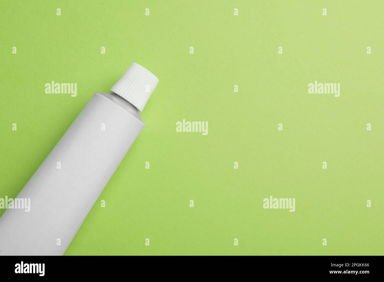 Blank white tube of ointment on light green background, top view. Space ...