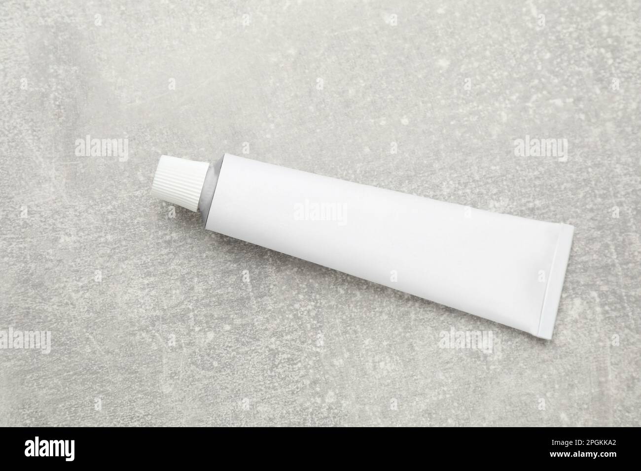 Blank white tube of ointment on light grey table, top view. Space for ...