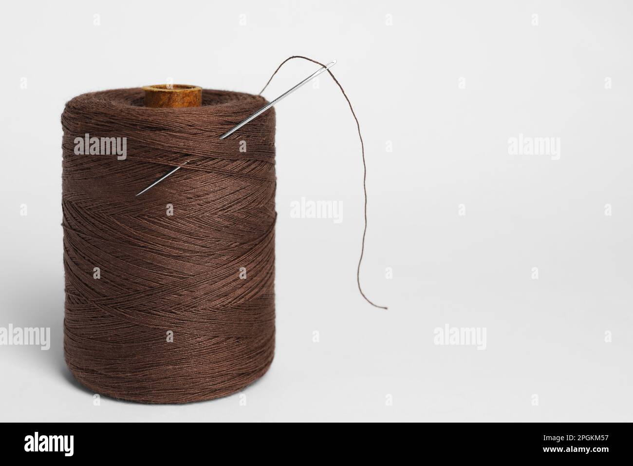 Brown sewing thread with needle on white background Stock Photo - Alamy