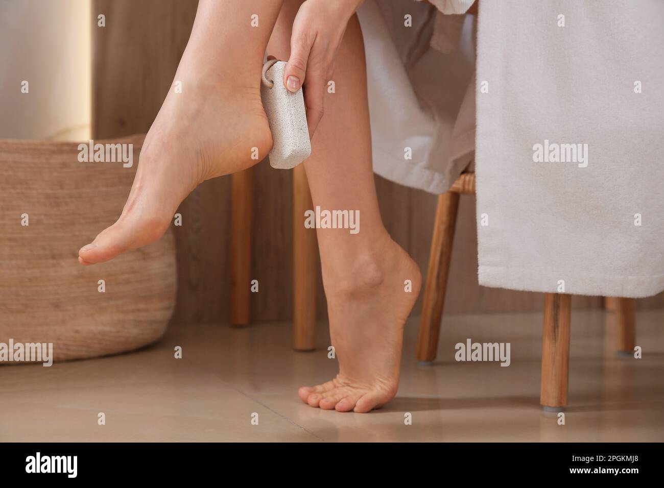 Woman using pumice stone for removing dead skin from feet indoors ...