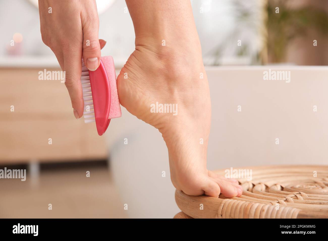 Woman using pumice stone for removing dead skin from feet in bathroom ...