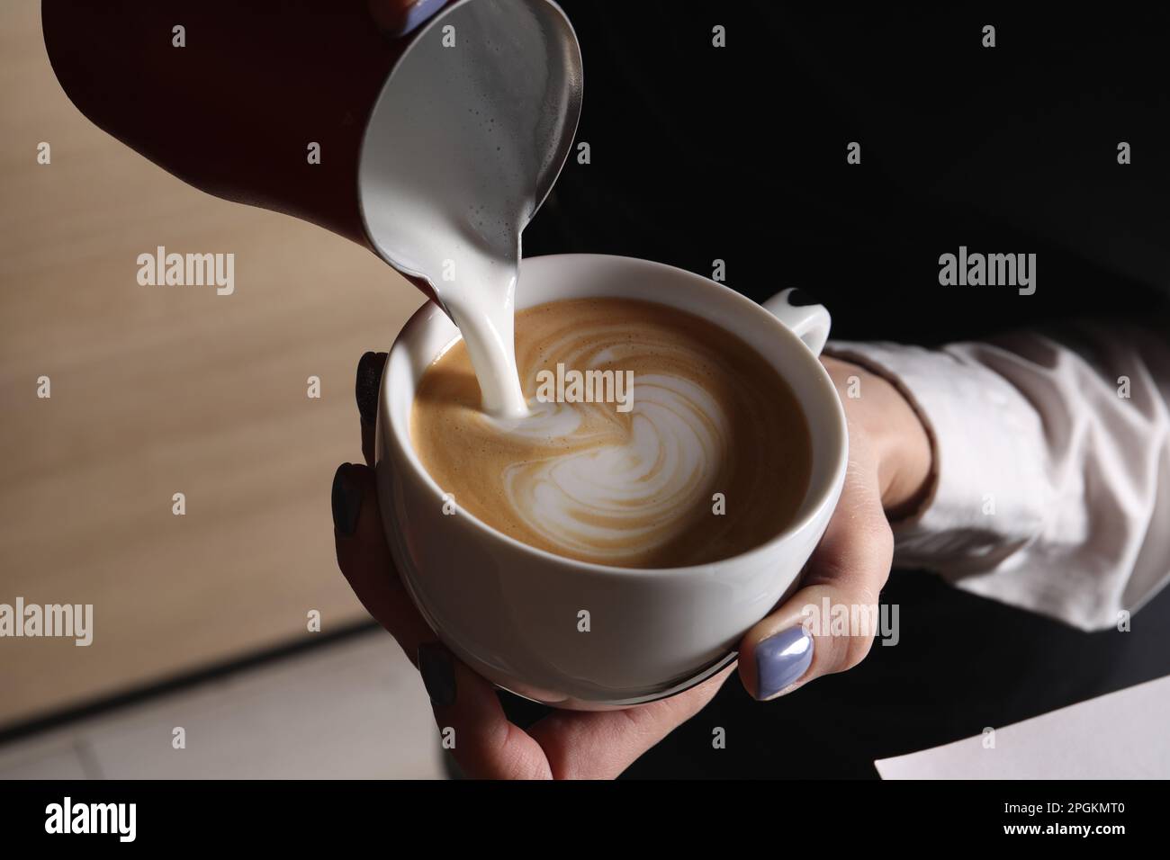 Barista pouring steamed milk from pitcher into cup of aromatic coffee ...