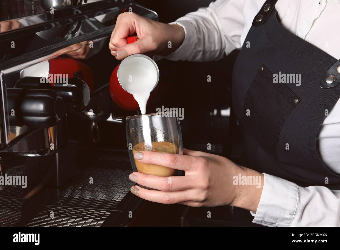 Barista pouring steamed milk from pitcher into glass cup of fresh ...