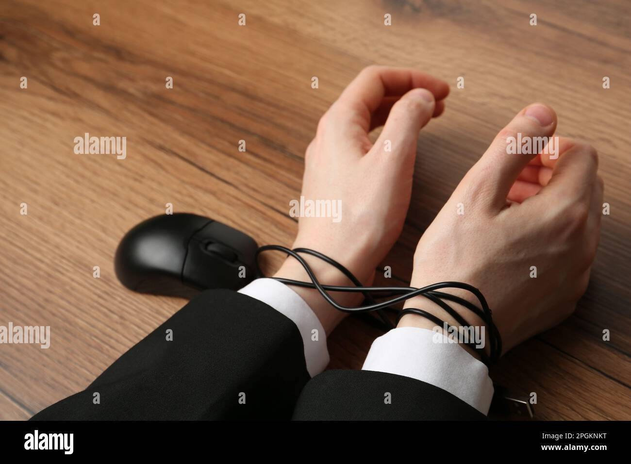 Man showing hands tied with computer mouse cable at wooden table ...