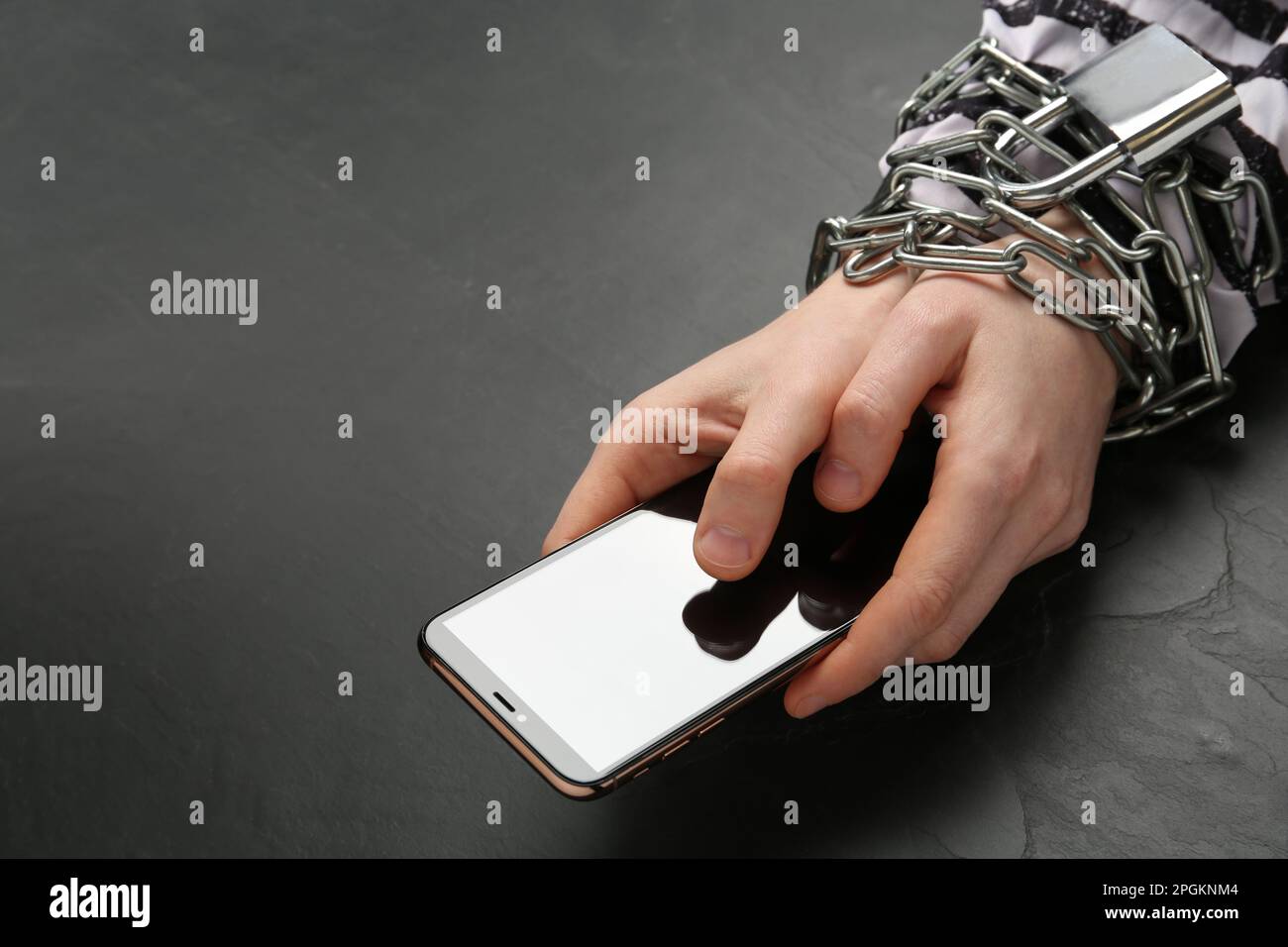 Prisoner holding smartphone in chained hands at black table, closeup ...