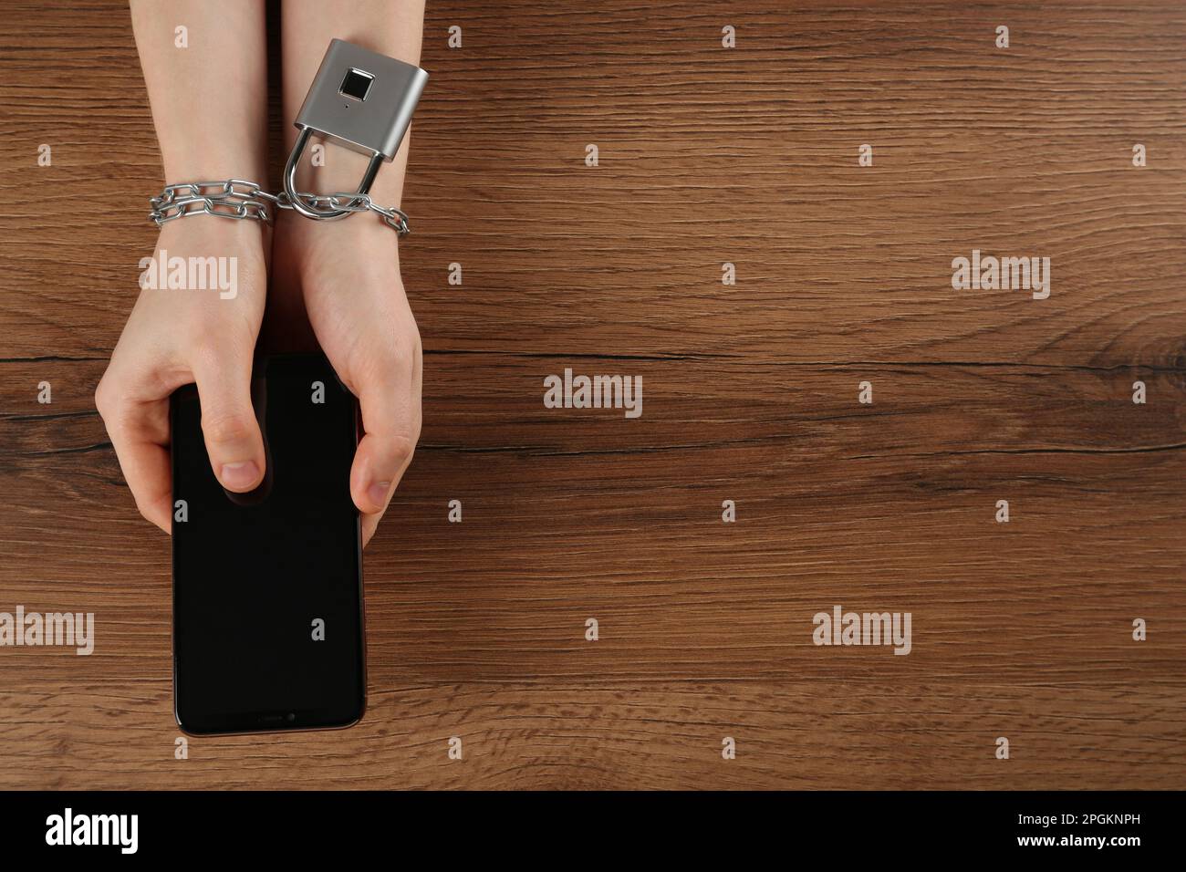 Woman holding smartphone in chained hands at wooden table, top view ...