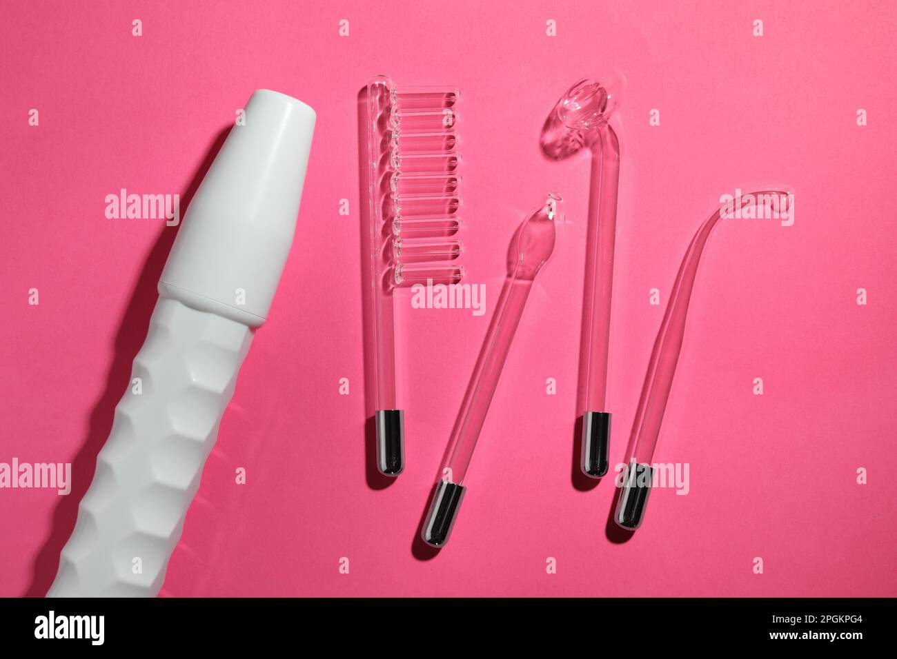 Modern darsonval with different nozzles on pink background, flat lay ...