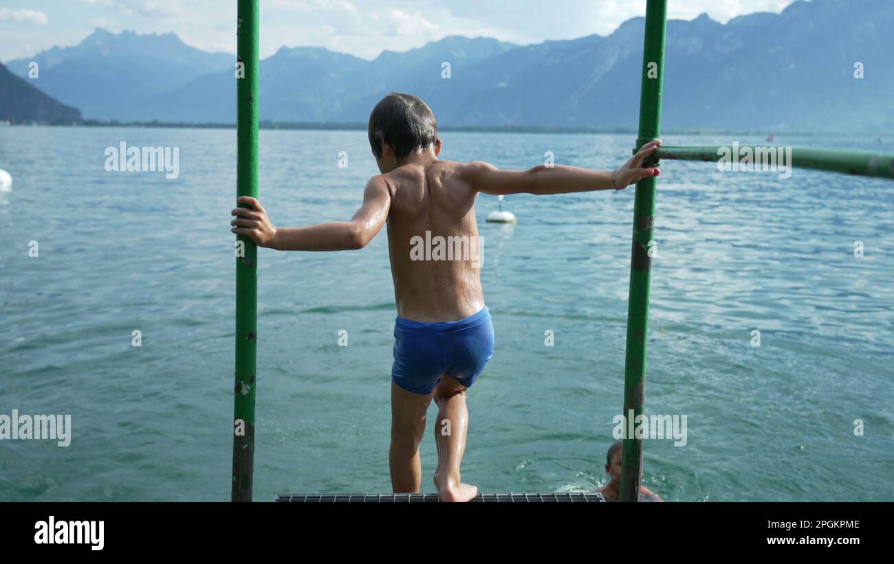 Back of children standing by lake pier overlooking mountains in ...