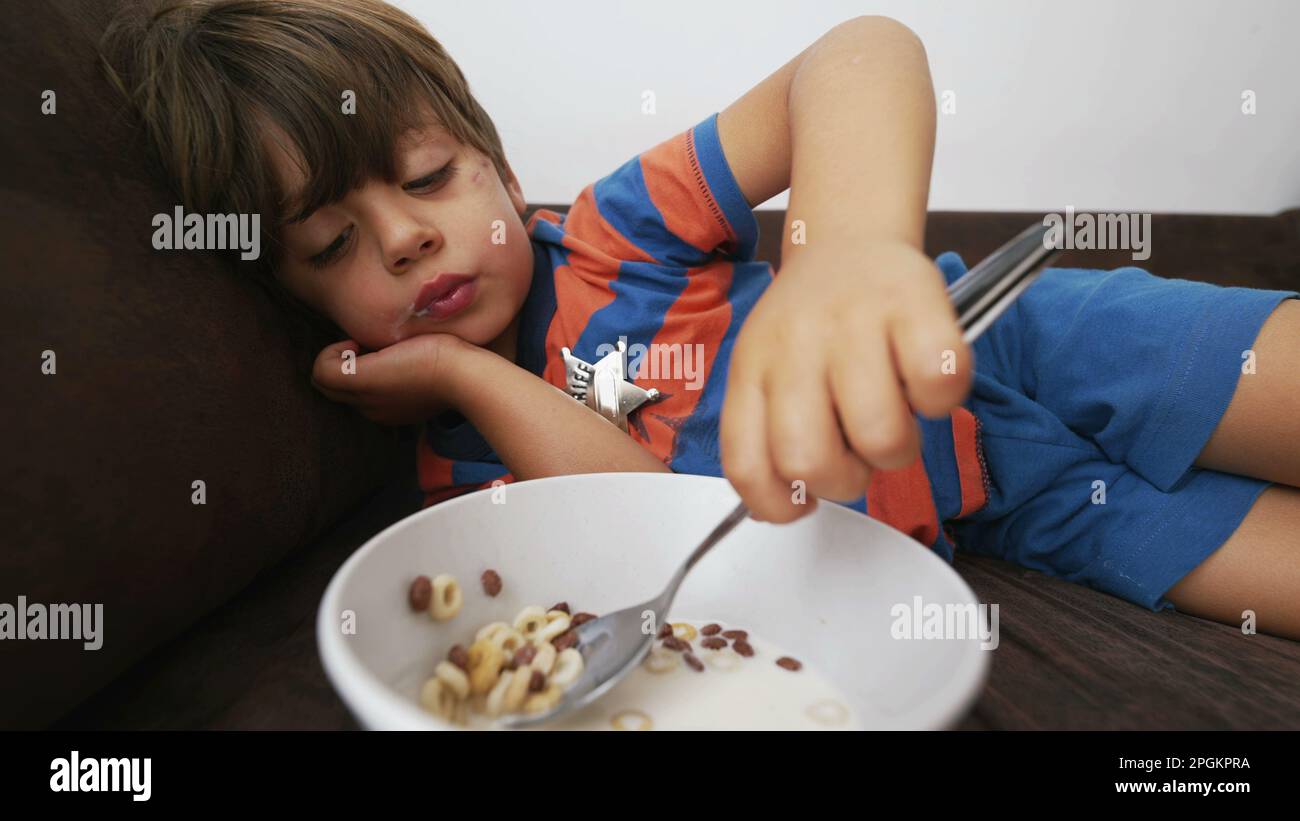 Child eating cereal with spoon. Breakfast food in milk and bowl lying ...