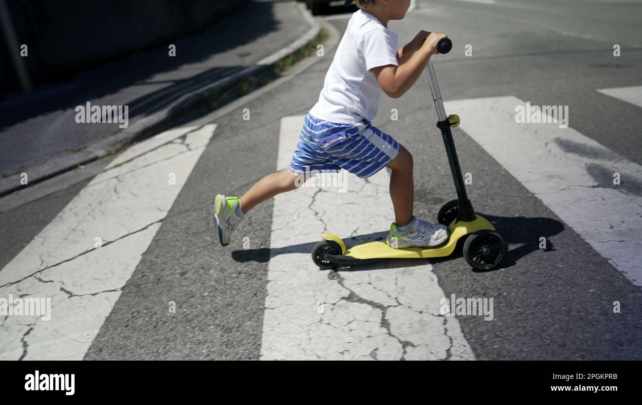 Child crossing crosswalk with toy scooter. Active little boy riding ...