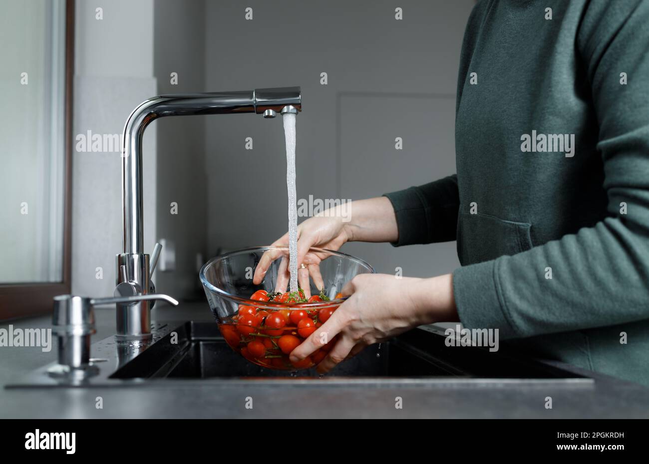Fresh red Cherry tomatoes in bowl under water stream in sink, woman ...