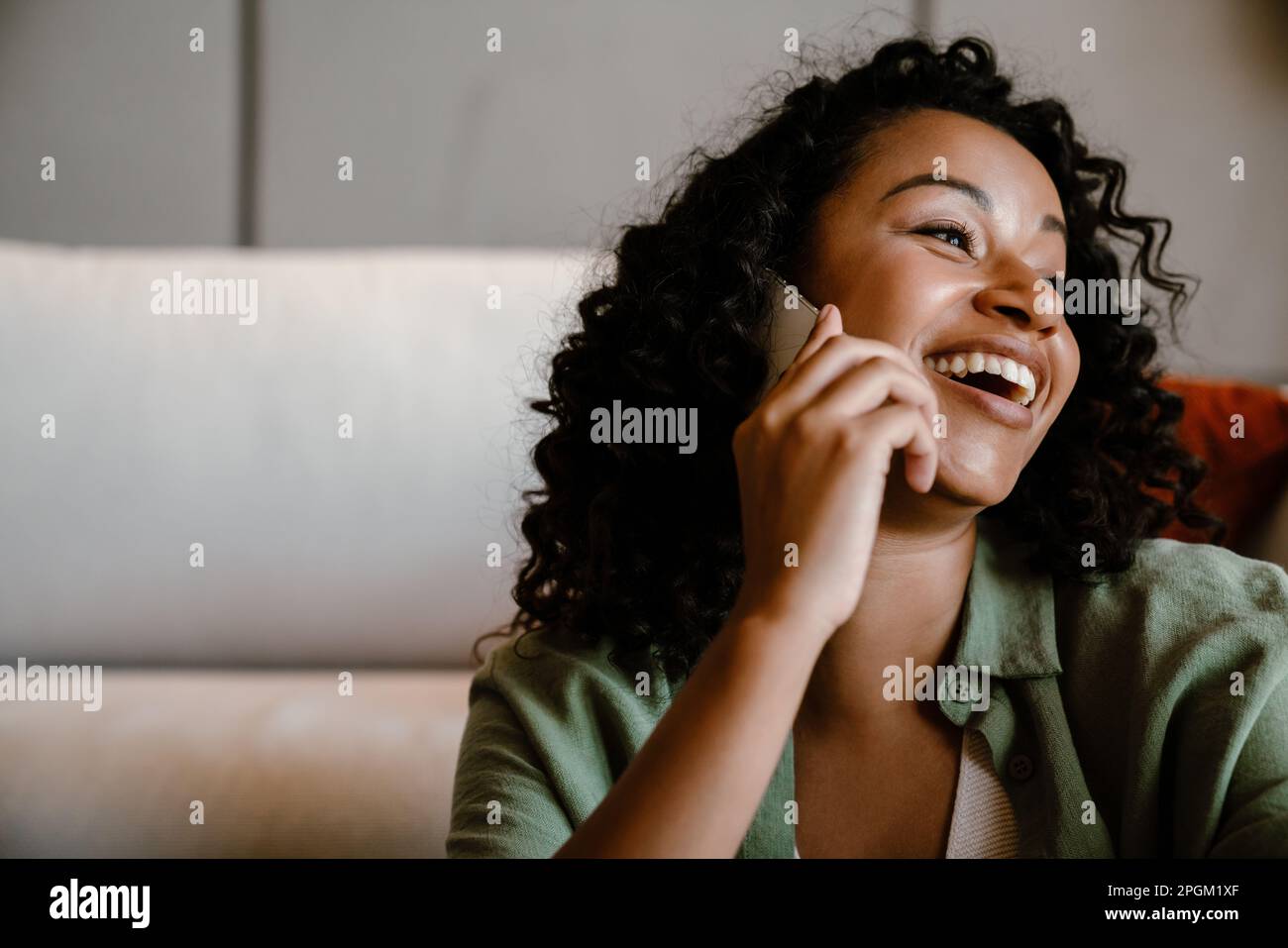 Excited young smiling african woman talking on mobile phone at home ...