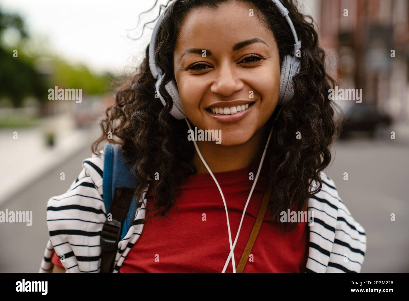 Young black woman in headphone looki camera while walking outdoors ...
