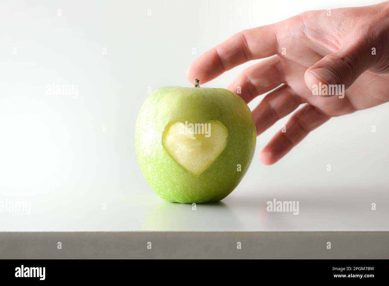 Hand picking apple with heart on white table and white isolated ...