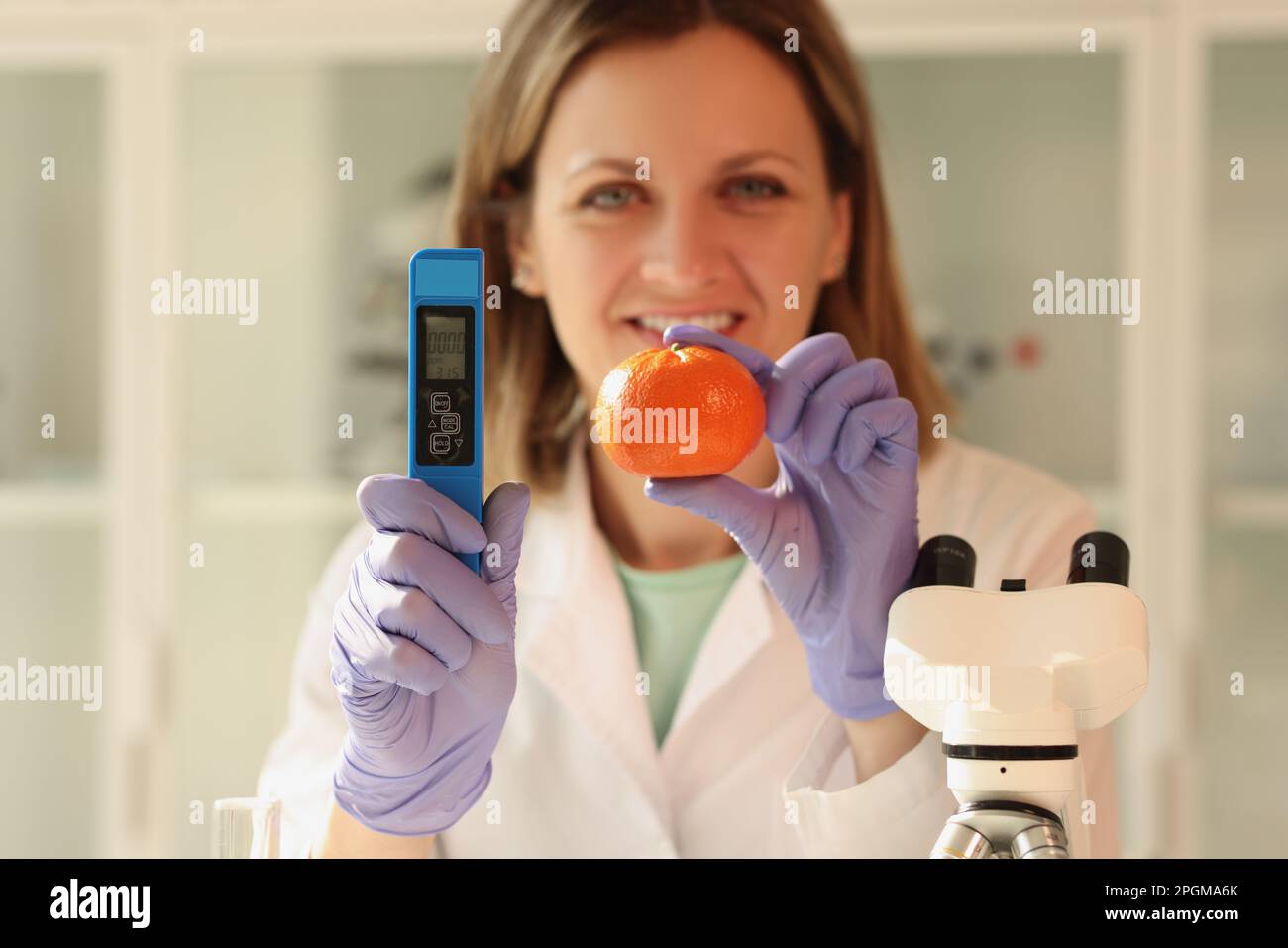 Positive laboratory worker holds mandarin and equipment Stock Photo - Alamy