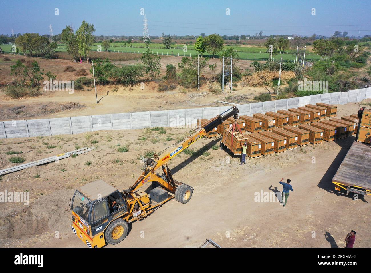 A crane lifting metal containers in a large solar panel field, with a ...