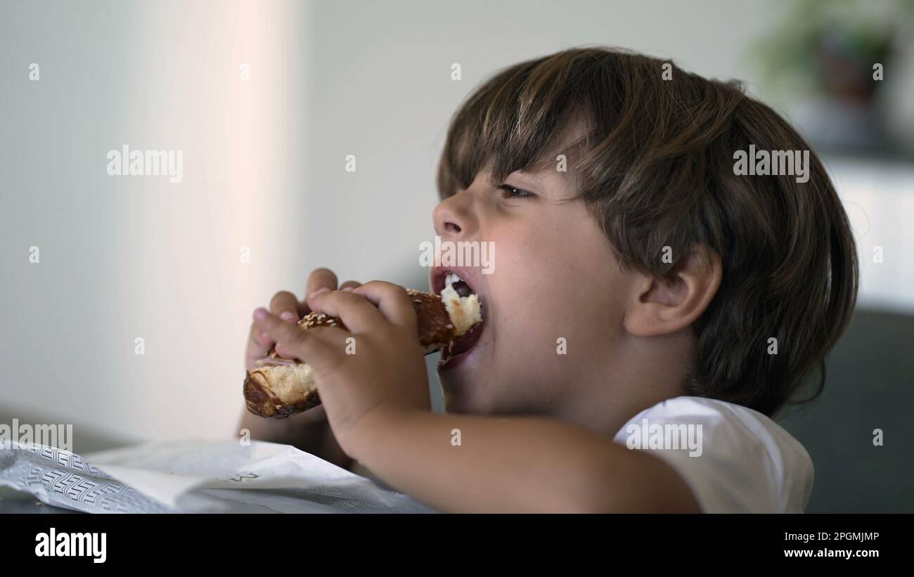 One little boy grabbing bread taking a bite of carb food seated at ...