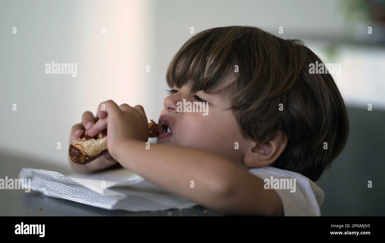 One little boy grabbing bread taking a bite of carb food seated at ...
