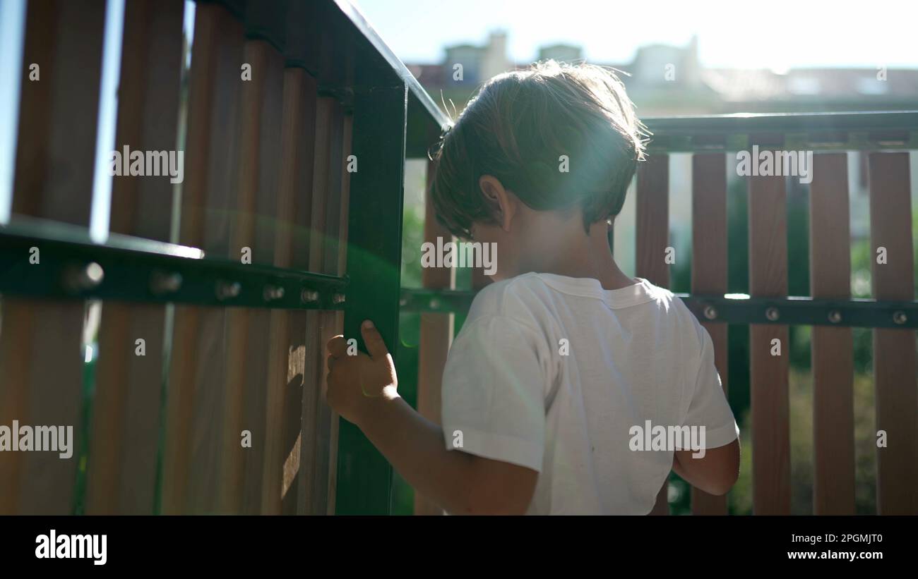One small boy standing by balcony fence staring outside from second ...