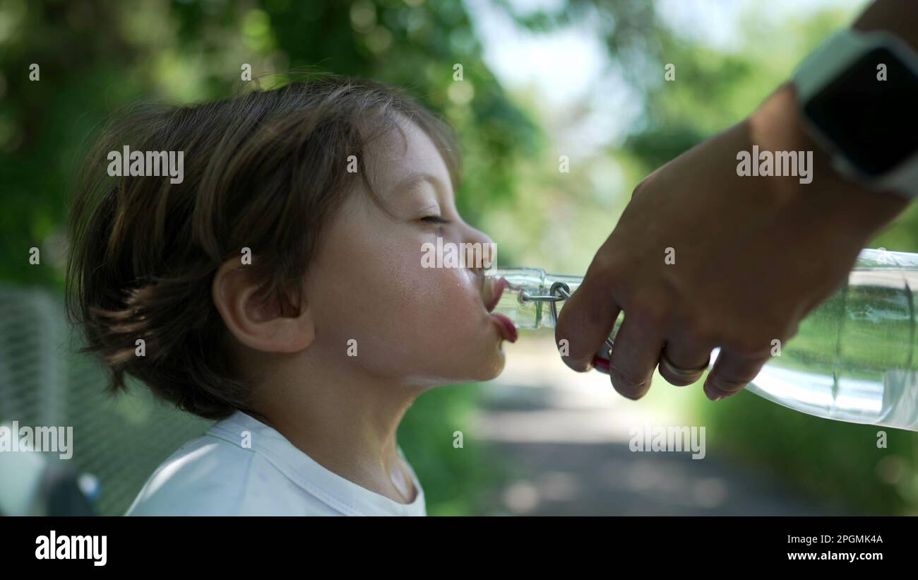 Little boy drinking water from glass bottle outside at park. Child hydrating drinks refreshing ...