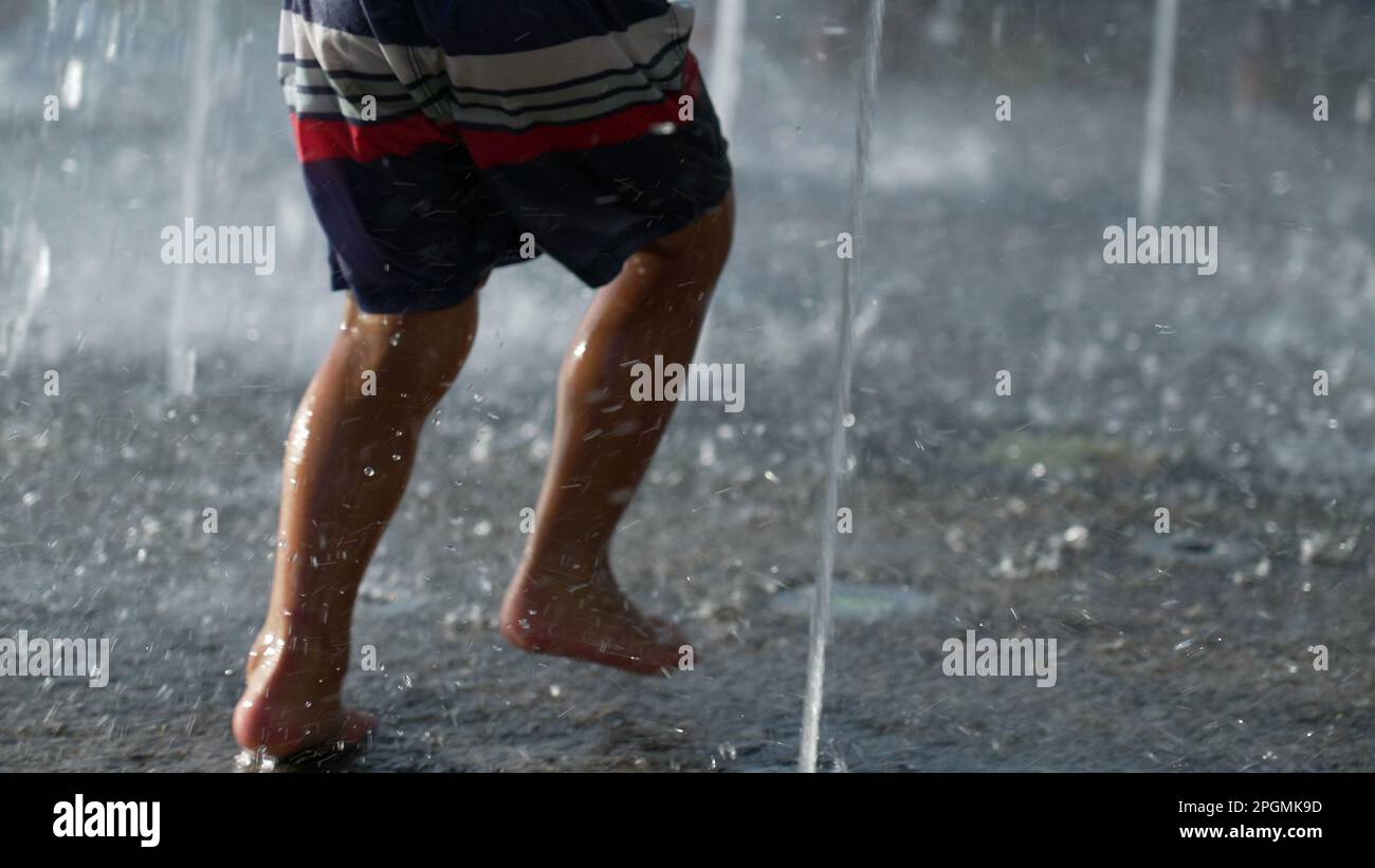 Little boy running toward water jet fountain. Kid having fun at water ...