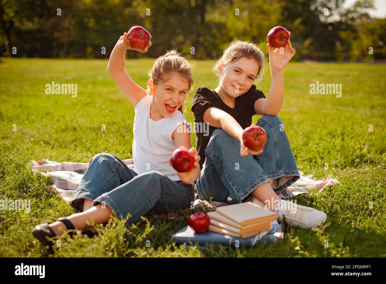 two girls play with red apples on green grass in park or school yard ...