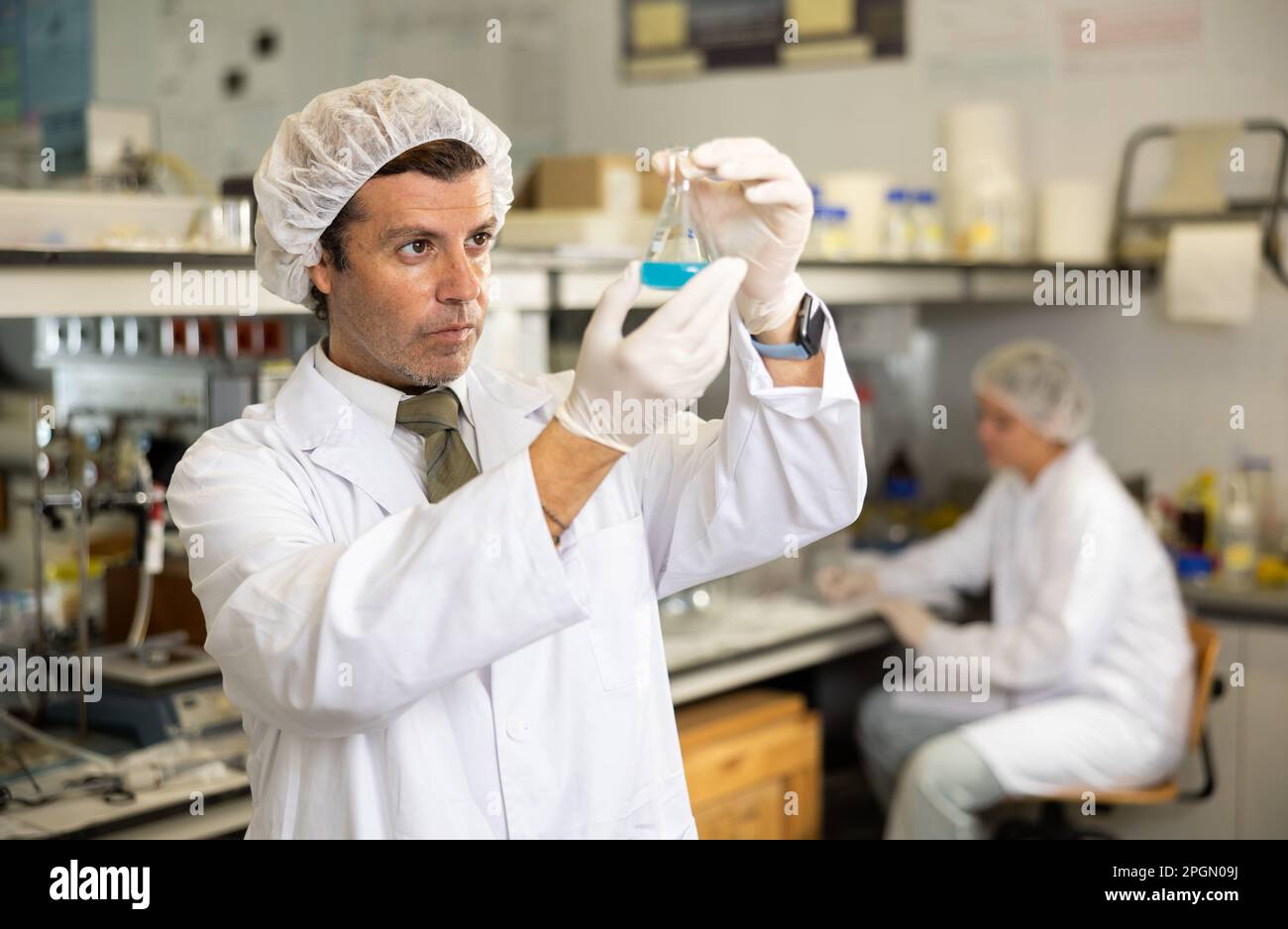 Skillful middle-aged male scientist in white coat pouring blue liquid ...