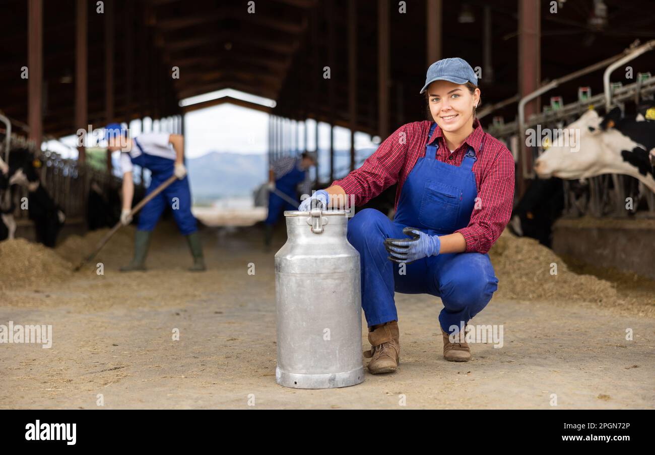 Cheerful hardworking woman farmer carrying milk can while walking ...