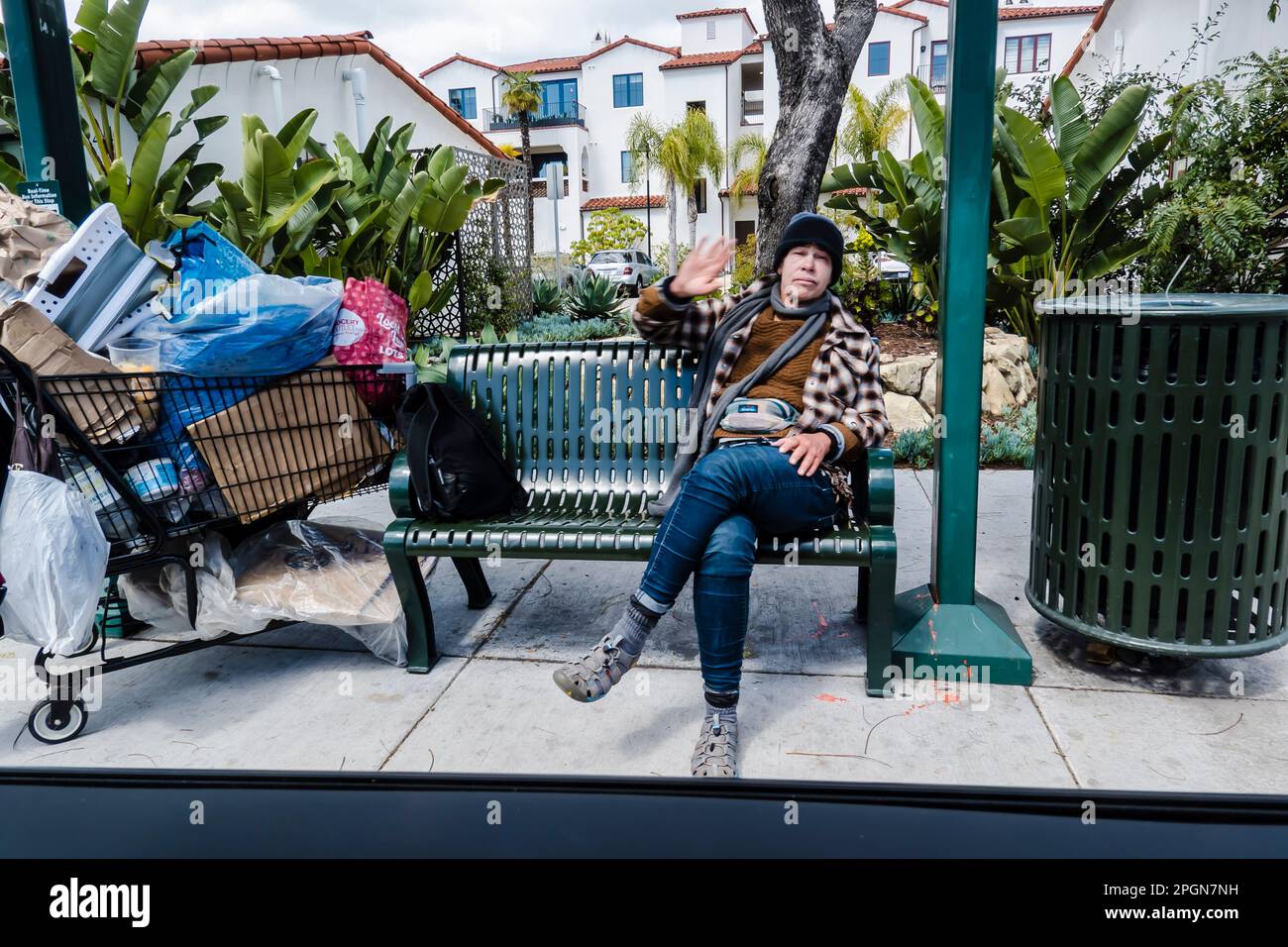 A homeless male sits on a bus stop bench with worldly possessions in a ...