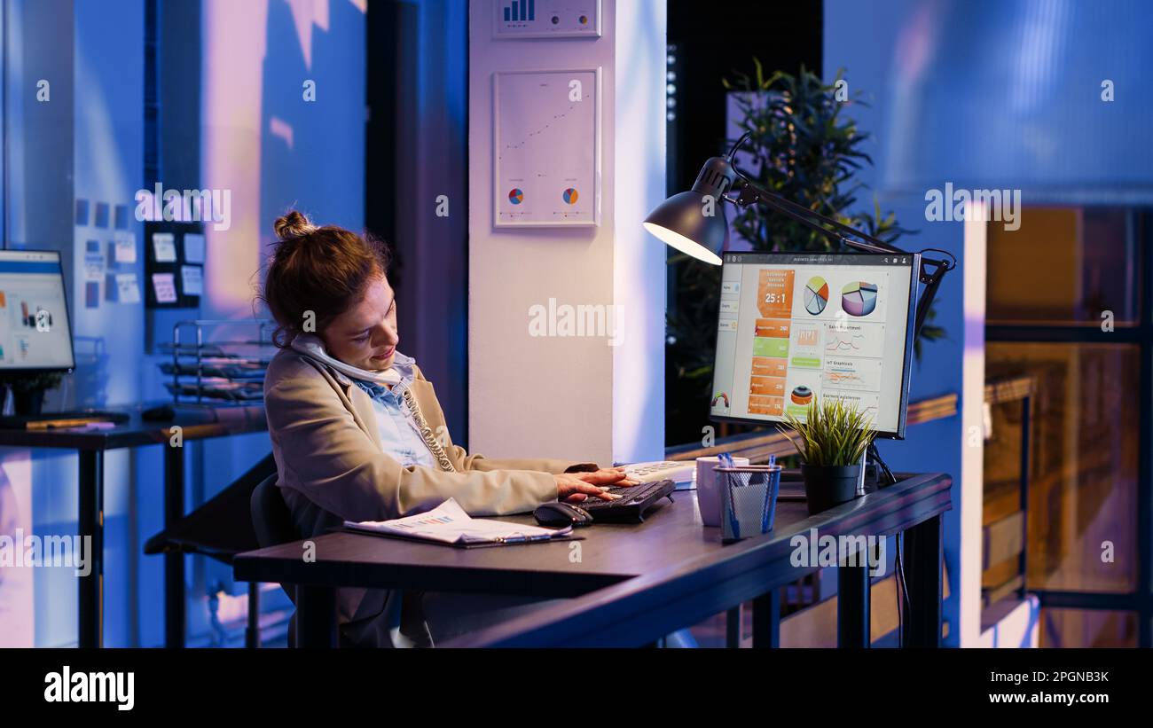 Business woman answering landline phone call at desk analyzing diagrams ...