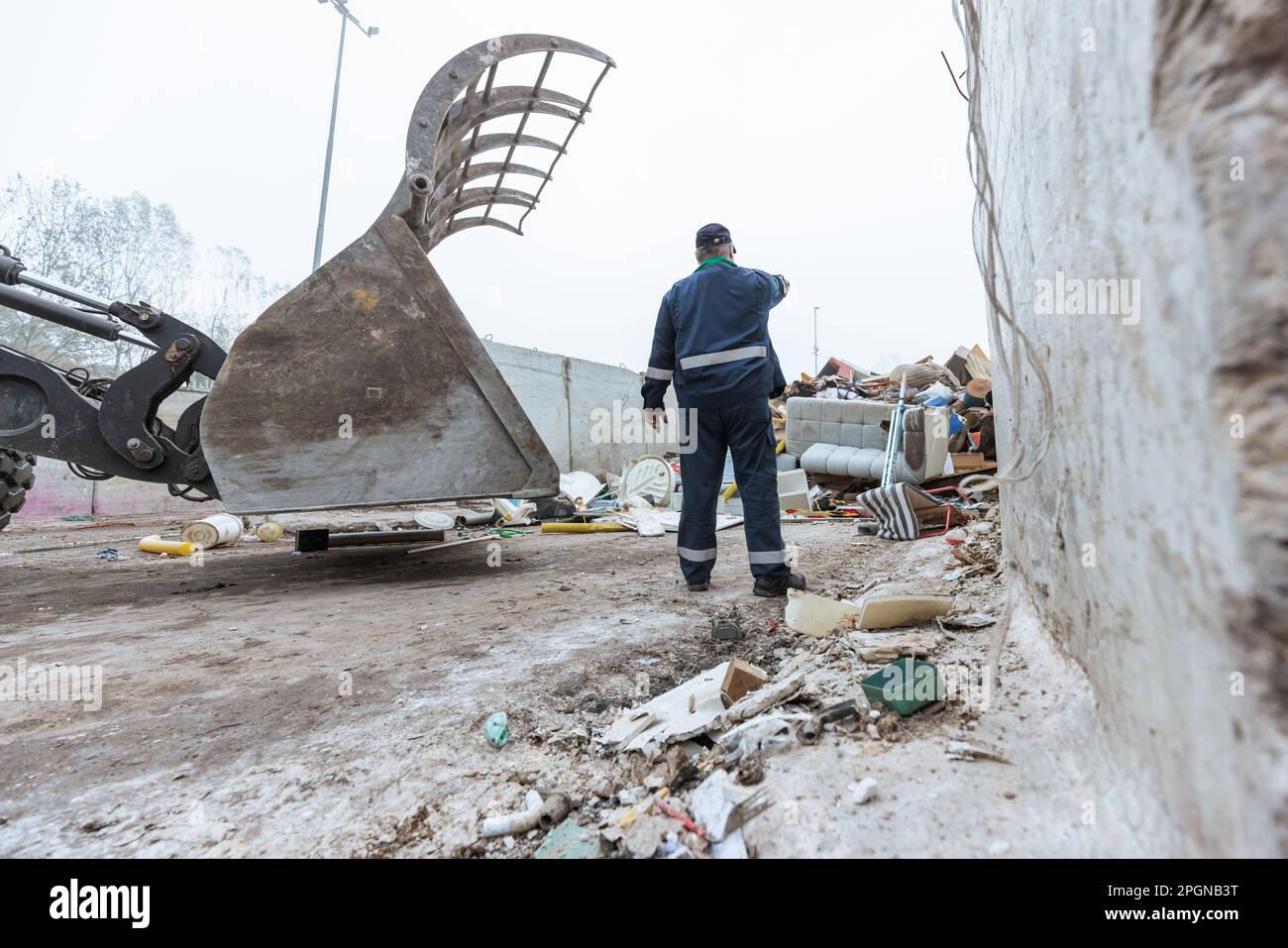 Landfill worker directing skid steer loader on the garbage heap, rear ...