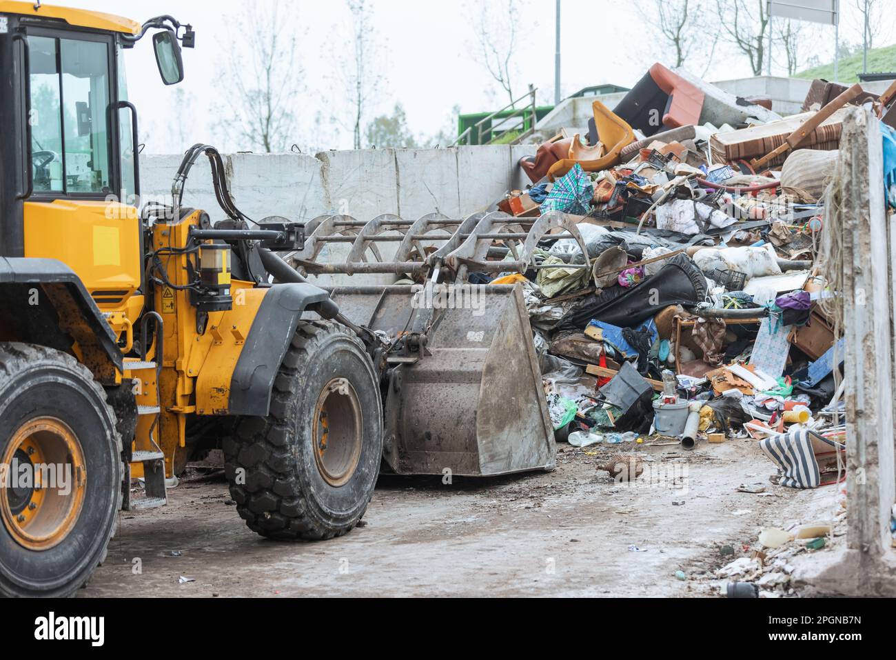 Yellow wheel loader, with lifted scrap grapple, moving along the ...