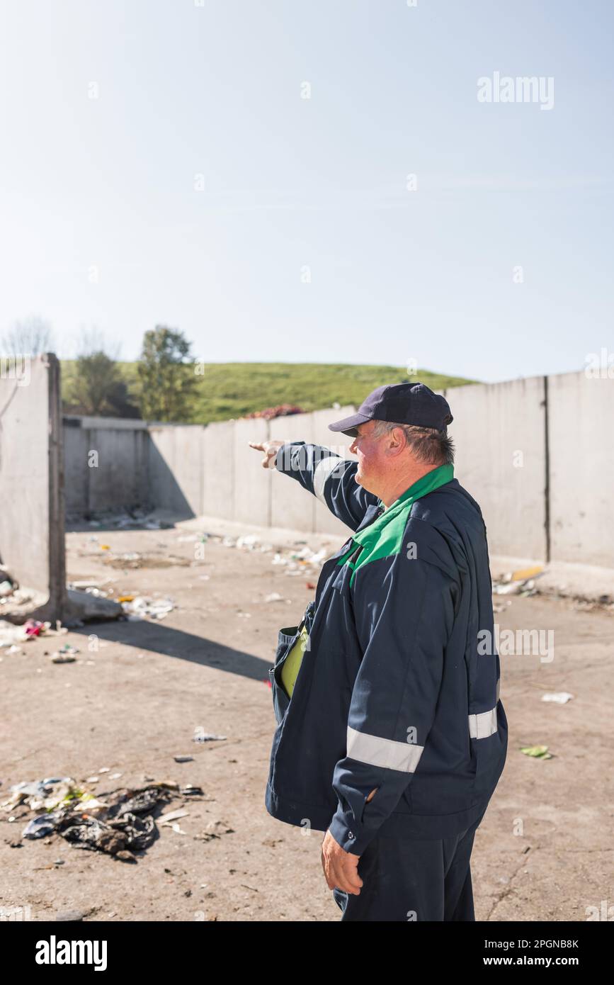 Landfill worker directing skid steer loader on the garbage heap. Waste ...
