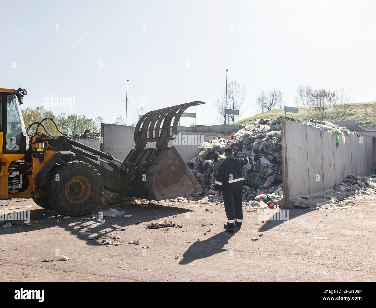 Landfill worker directing skid steer loader on the garbage heap. Waste ...