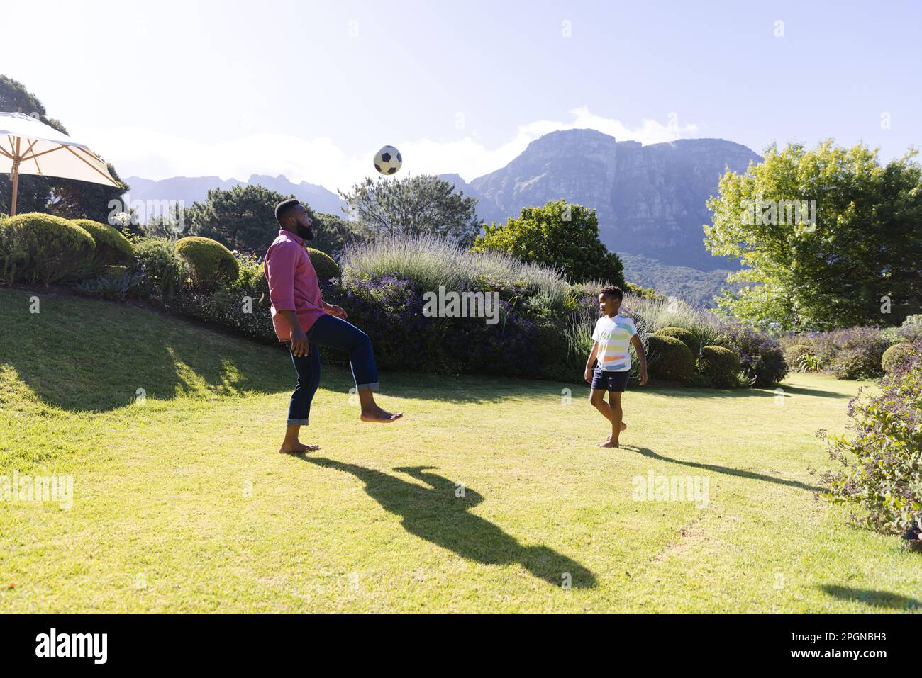 Happy african american father and son playing football in garden ...