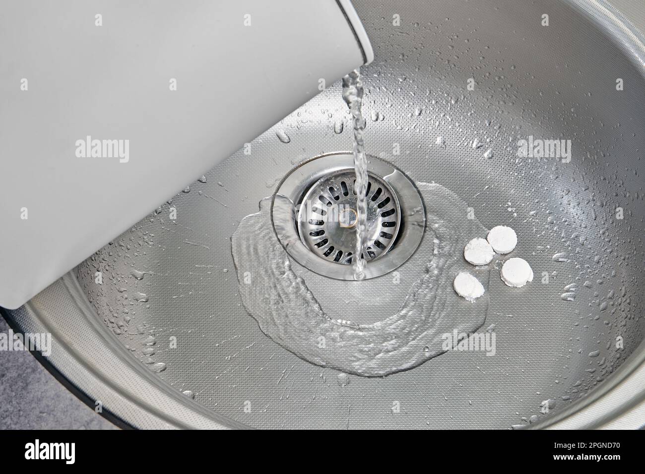 Hot water is poured from a white electric kettle into a metal kitchen ...