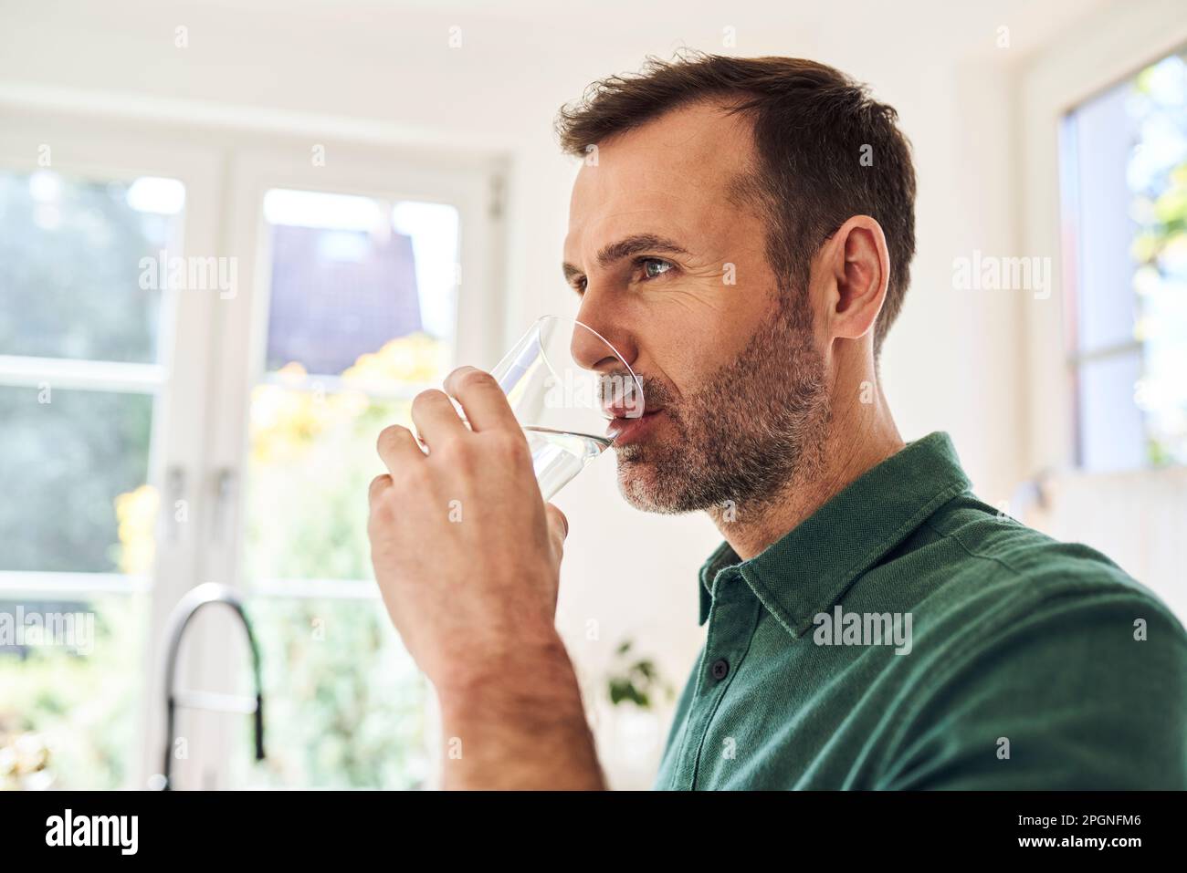 Man drinking glass of water standing in the kitchen Stock Photo - Alamy